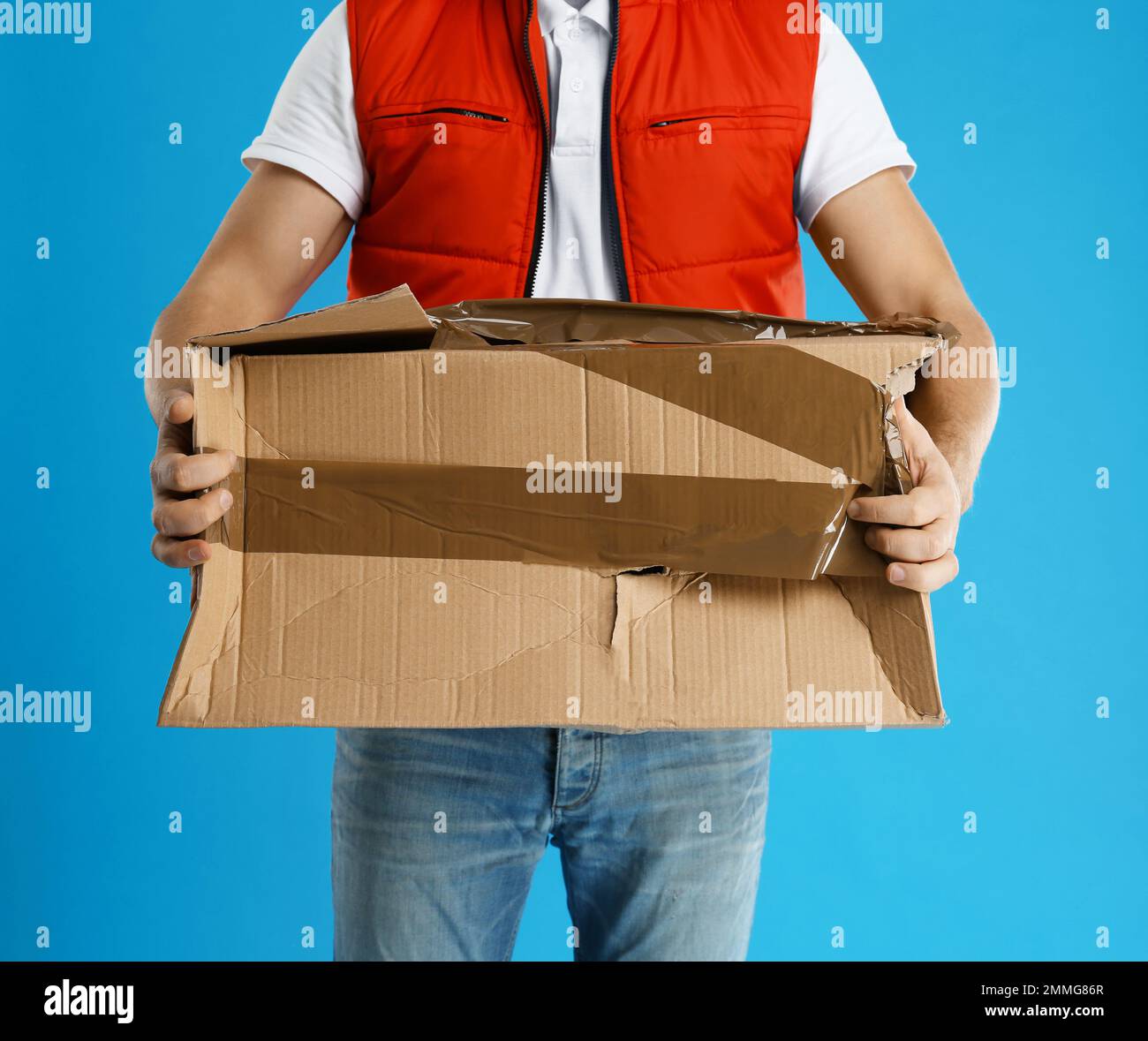 Courier with damaged cardboard box on blue background, closeup. Poor ...
