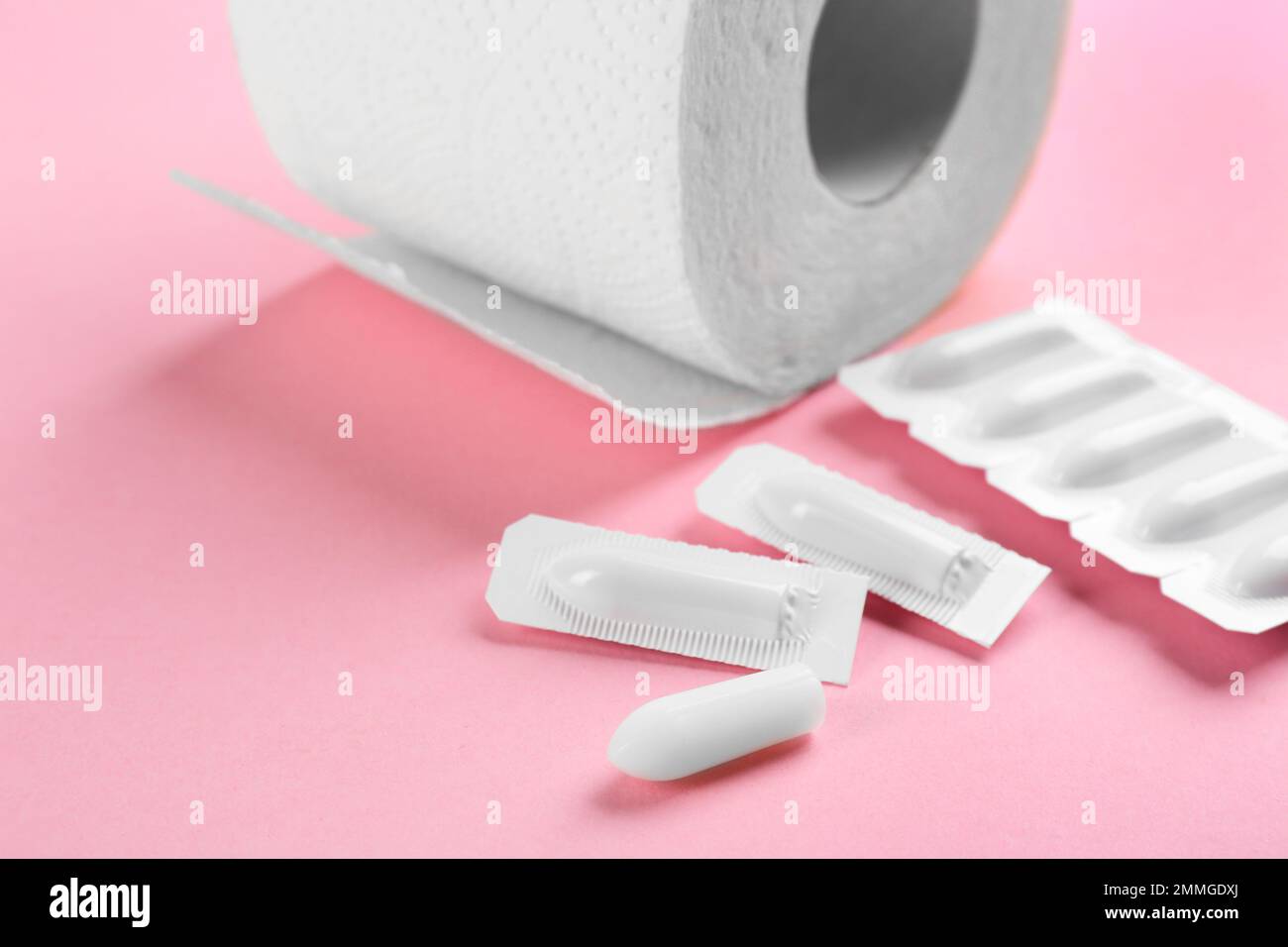 Suppositories and toilet paper on pink background, closeup view ...