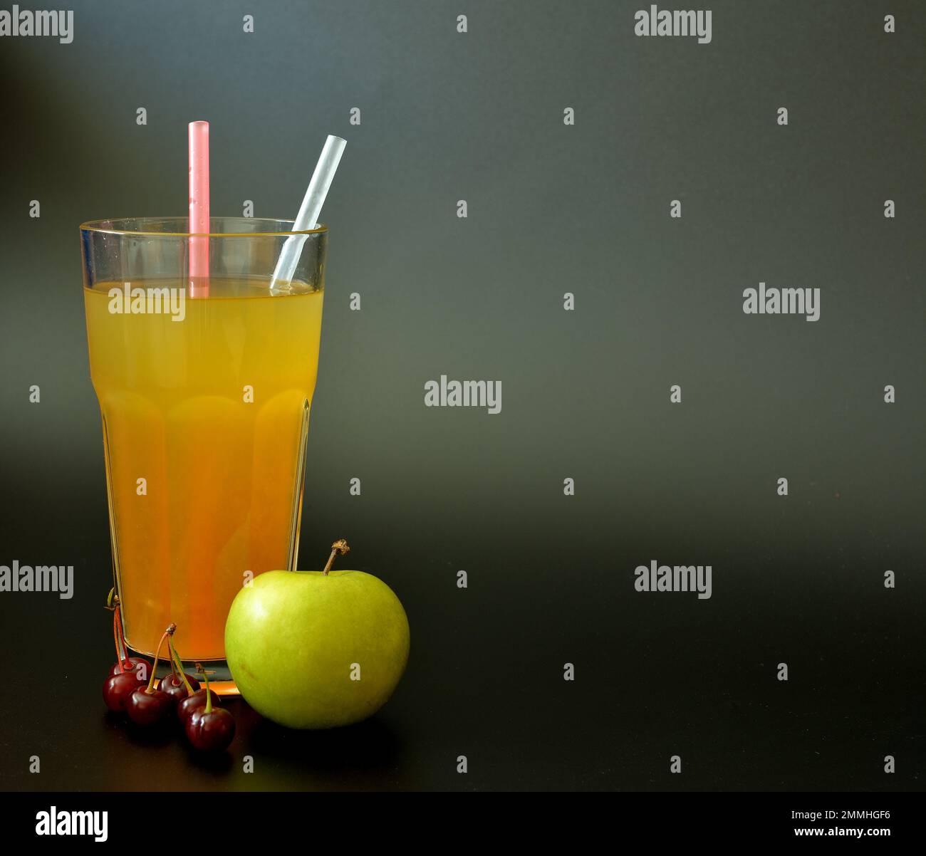 A tall glass of fruit juice with straws on a black background, next to ...