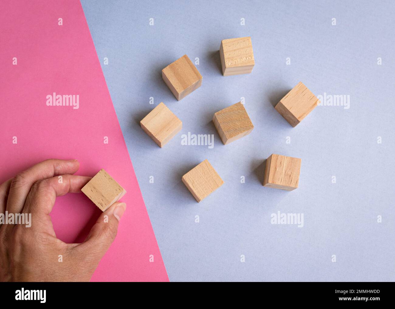 Wooden blocks on blue and pink background with a hand picking one of ...