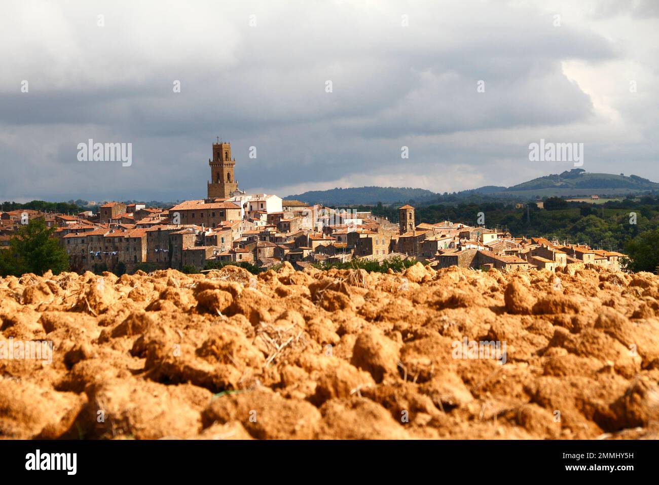 View across red clods of a ploughed field to medieval Tuscanian town ...