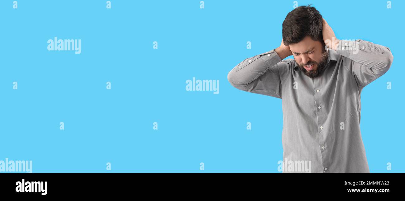 Young man suffering from loud noise on light blue background with space ...