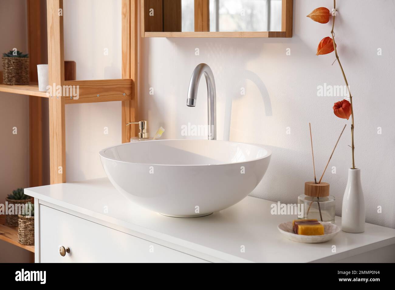 Ceramic sink, vase with plant branch and bath accessories on drawers in ...