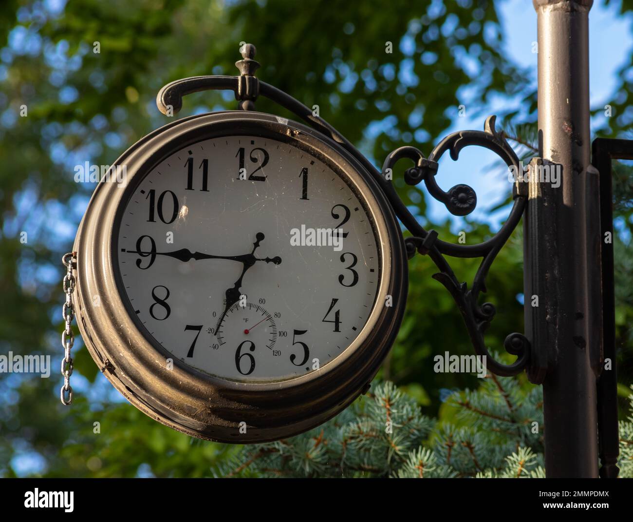 Old fashioned vintage street clock against greenl trees and blue sky ...
