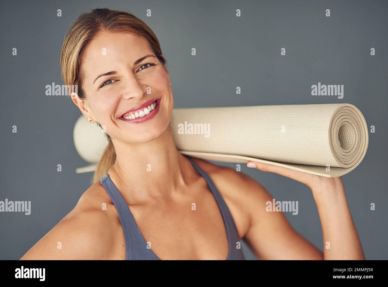 Yoga gives you more energy. a woman holding her yoga mat against a grey ...