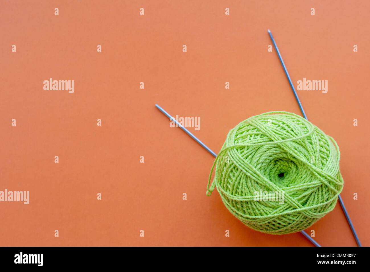 Green knitting yarn ball and knitting needles top view on an orange ...