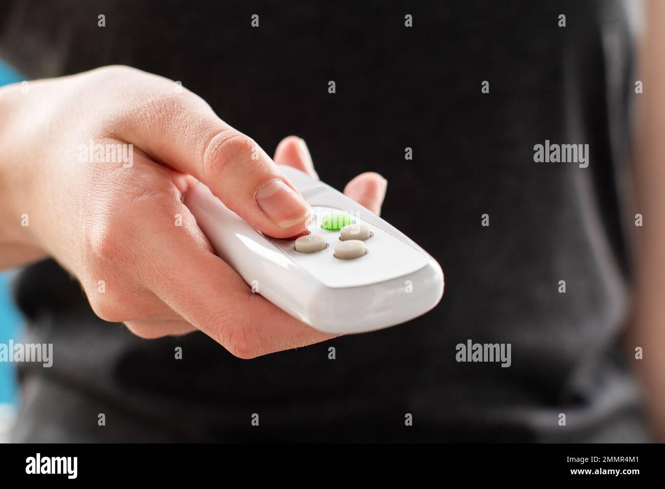 Close-up female hand hold a white remote control to switch channels on ...
