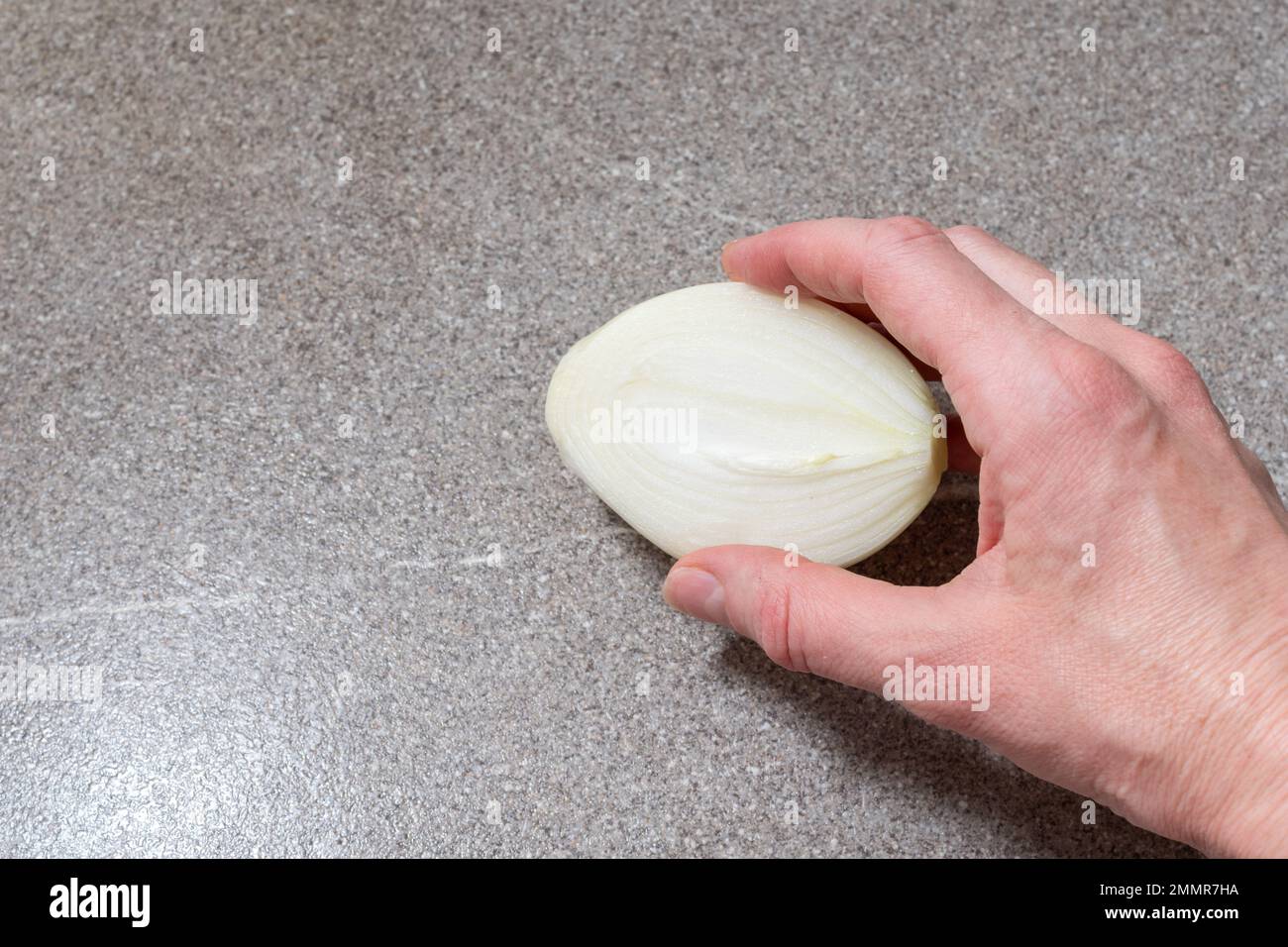 Female hand holding half of raw onion on gray trending background, copy ...