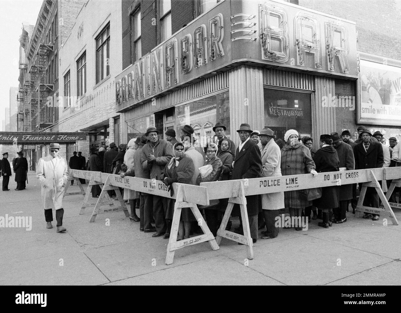 A crowd of mourners stand behind police barricades as they wait to ...