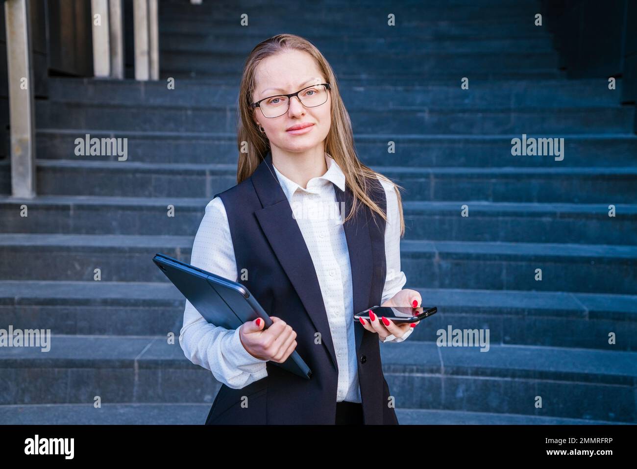 Woman realtor in jacket walks down stairs with laptop and phone in her ...
