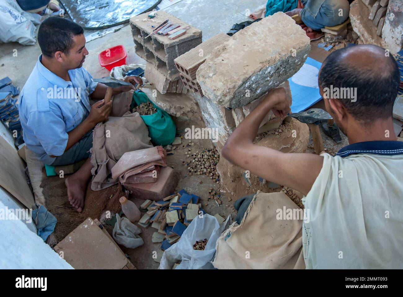 Workers cutting ceramic tiles into cube shapes using brick hammers at a ...