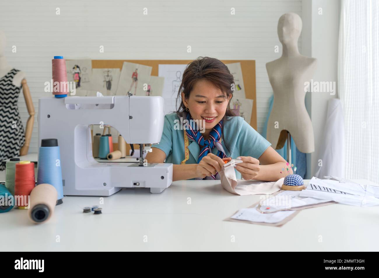 Young dressmaker cut the thread with scissors after finish sewing on a machine. Asian woman ...