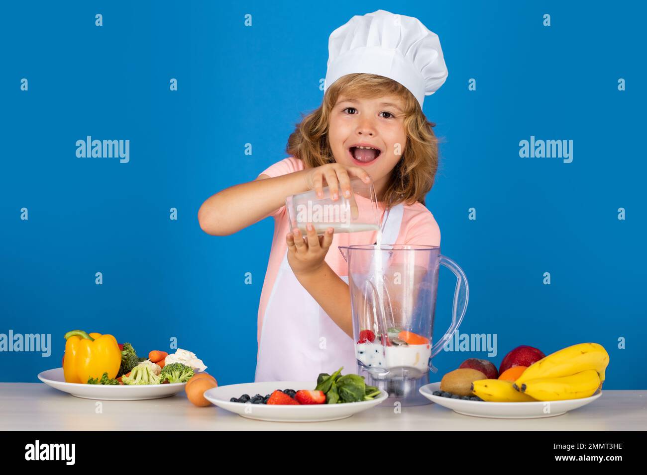 Child chef cook prepares milk shake smoothie in isolated blue studio ...