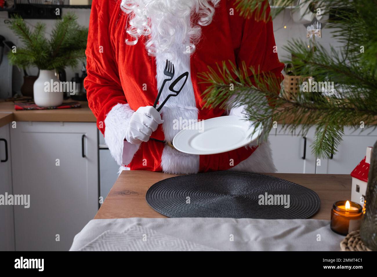 Santa Claus sets the table at home in the white kitchen, puts a plate ...