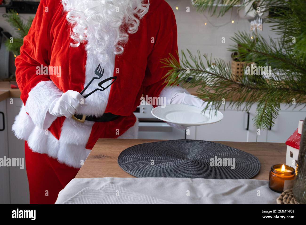 Santa Claus sets the table at home in the white kitchen, puts a plate ...