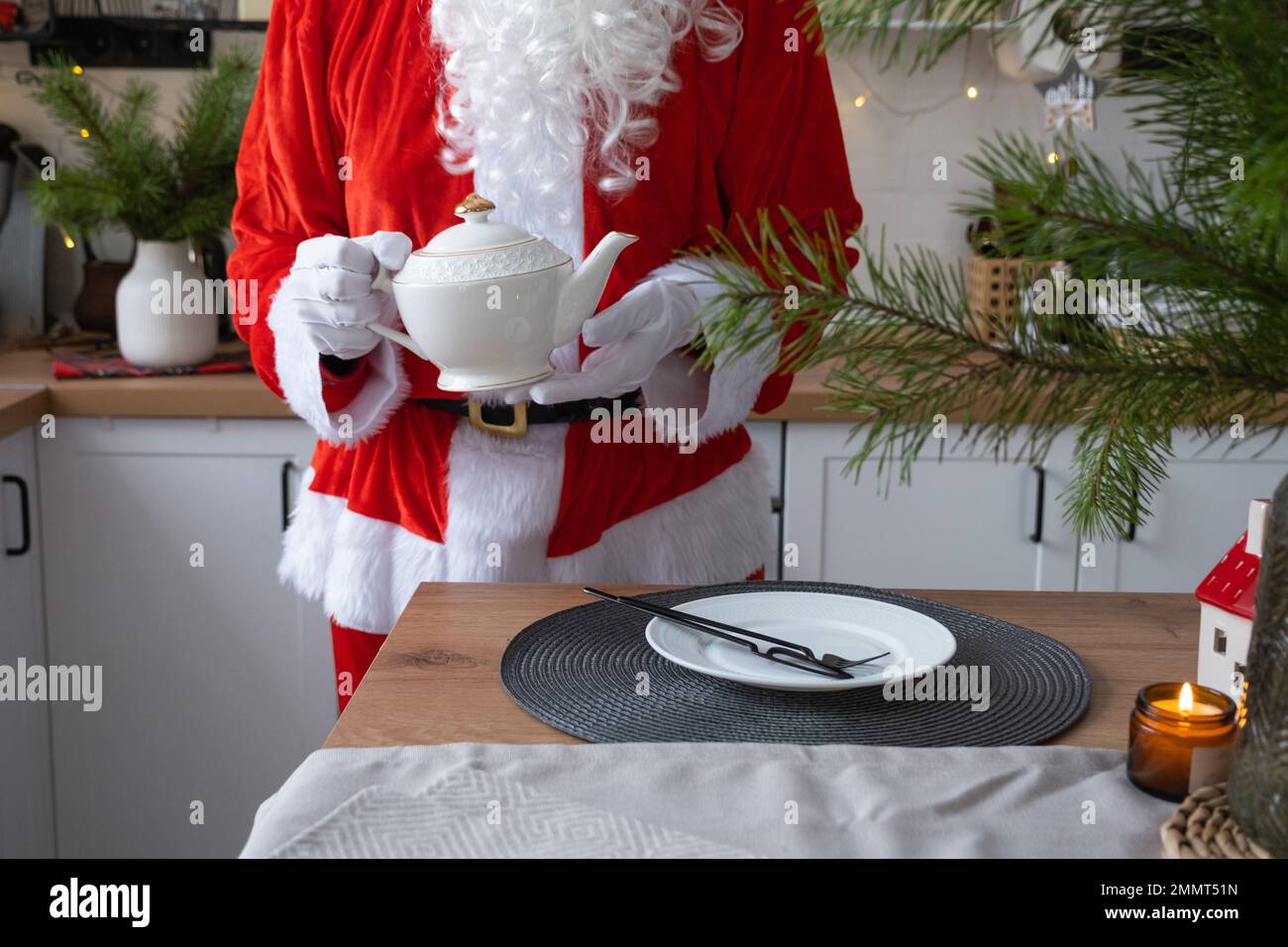 Santa Claus sets the table at home in the white kitchen, puts a plate ...