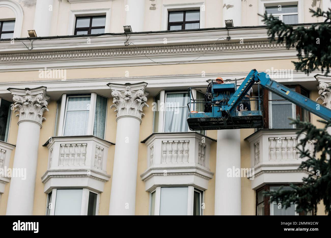 Worker in cradle of crane, restoring old facade of historic building ...