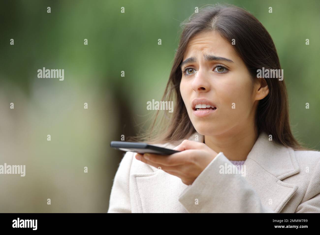 Worried woman dictating message on cell phone in a park in winter Stock ...