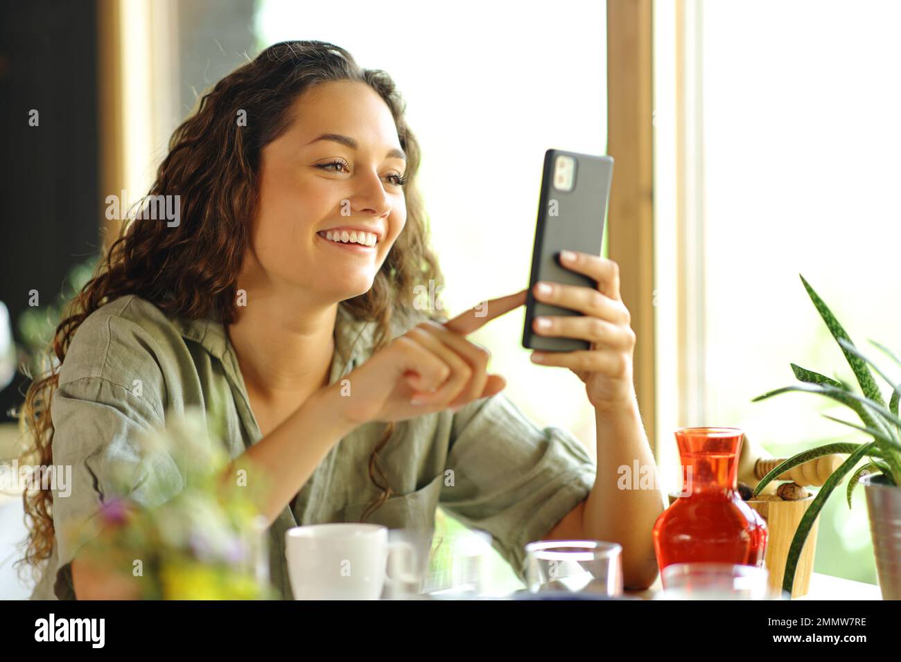 Happy woman smiling using phone in a restaurant Stock Photo - Alamy