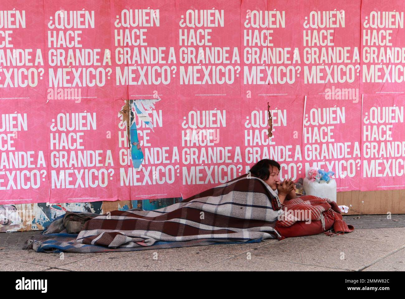 An homeless man rests under signs carrying the Spanish message: "Who ...