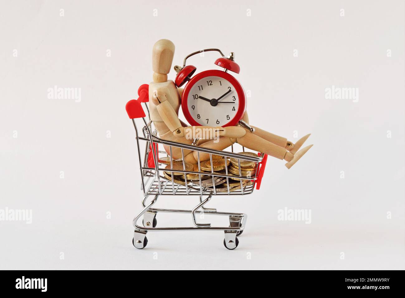Wooden mannequin sitting in shopping cart with alarm clock on white ...