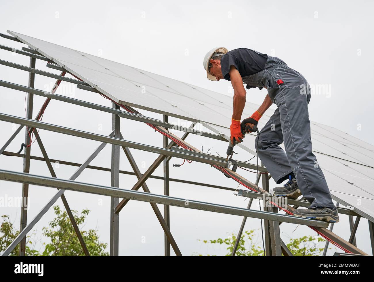 Worker fixing metal beams with electric drill for solar panels. Man ...