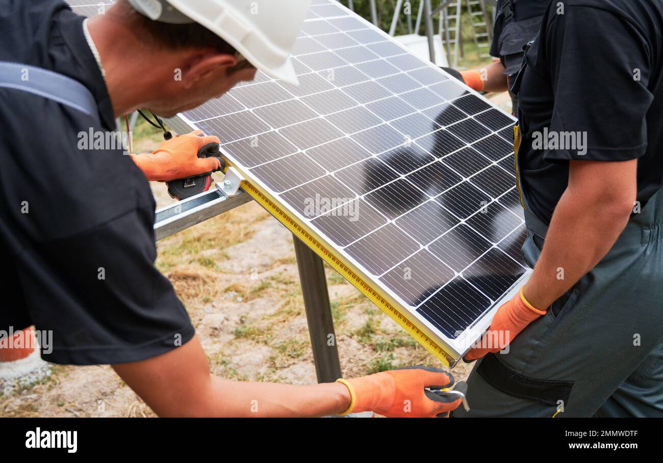 Worker measuring solar panel with measuring tape while his colleagues ...