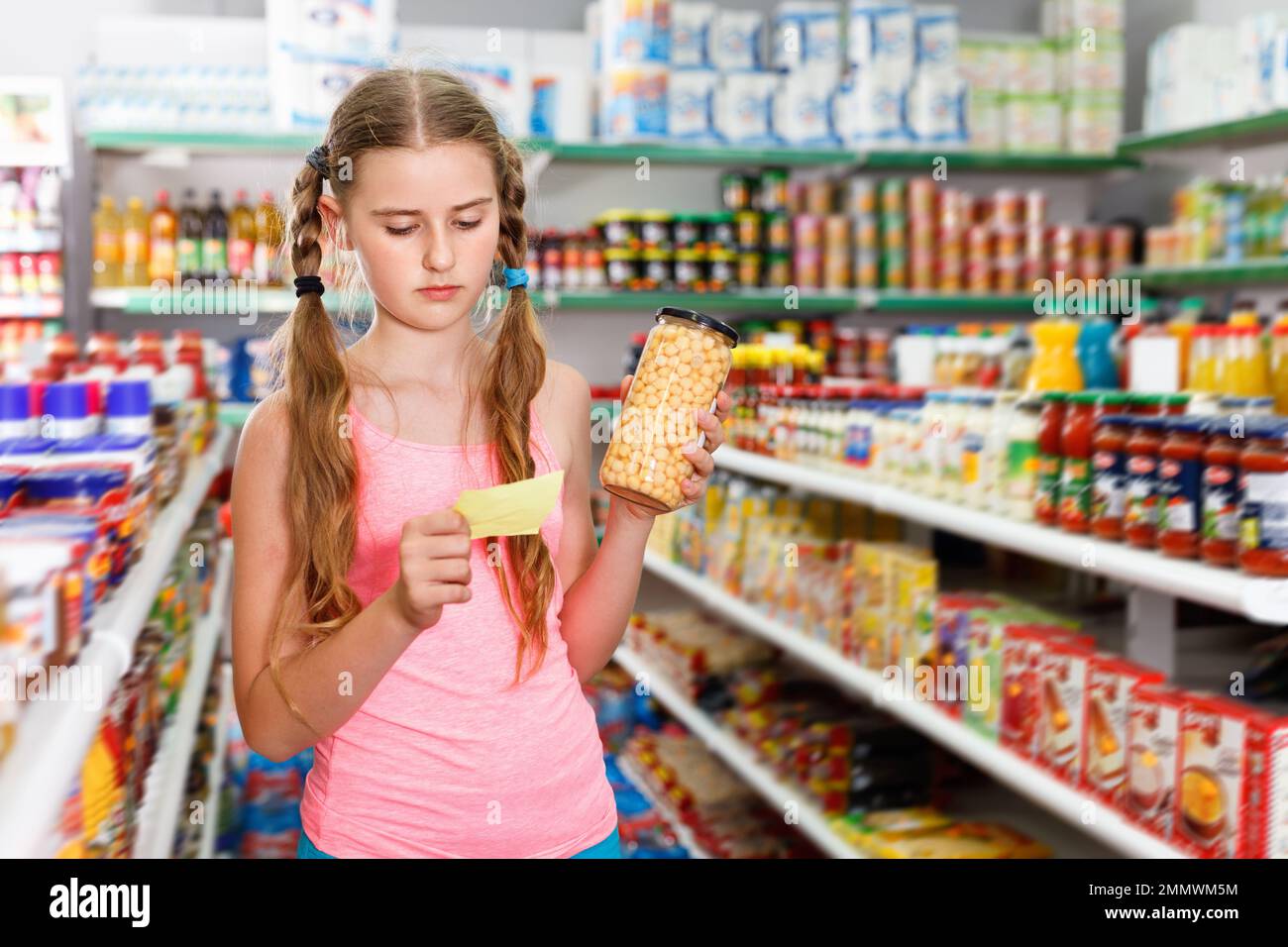 Positive tween girl choosing food products on shopping list in ...