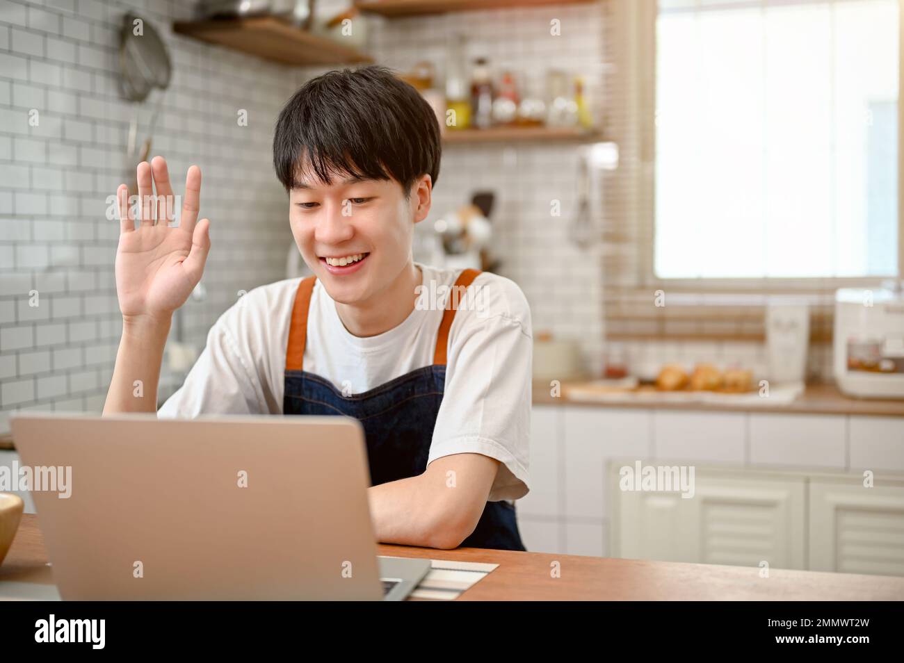 Happy and cute young Asian man in apron using laptop, having an online ...