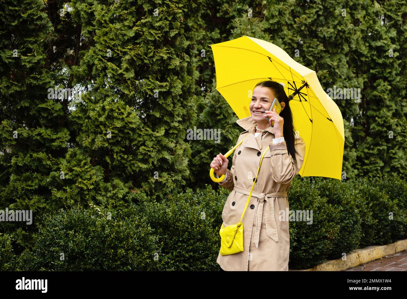 Happy Senior Woman In Yellow Rain Coat With Yellow Umbrella Is Talking