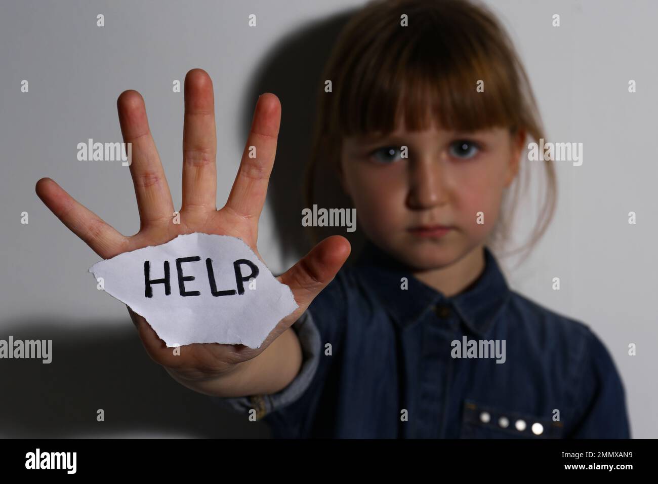 Abused little girl with sign HELP near white wall, focus on hand ...