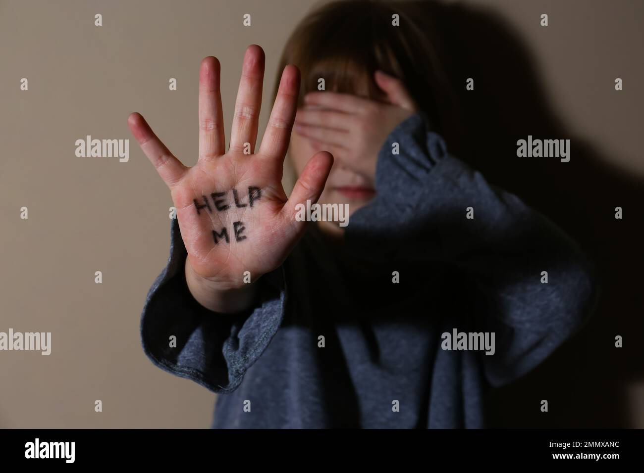 Crying little girl showing palm with phrase HELP ME near beige wall ...