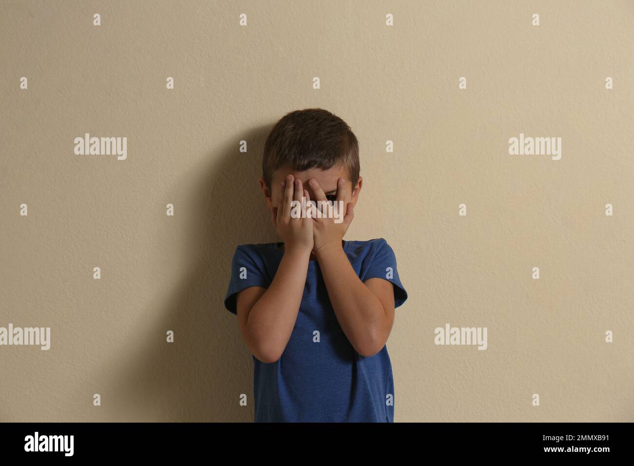 Scared little boy closing face by hands on yellow background. Child in ...
