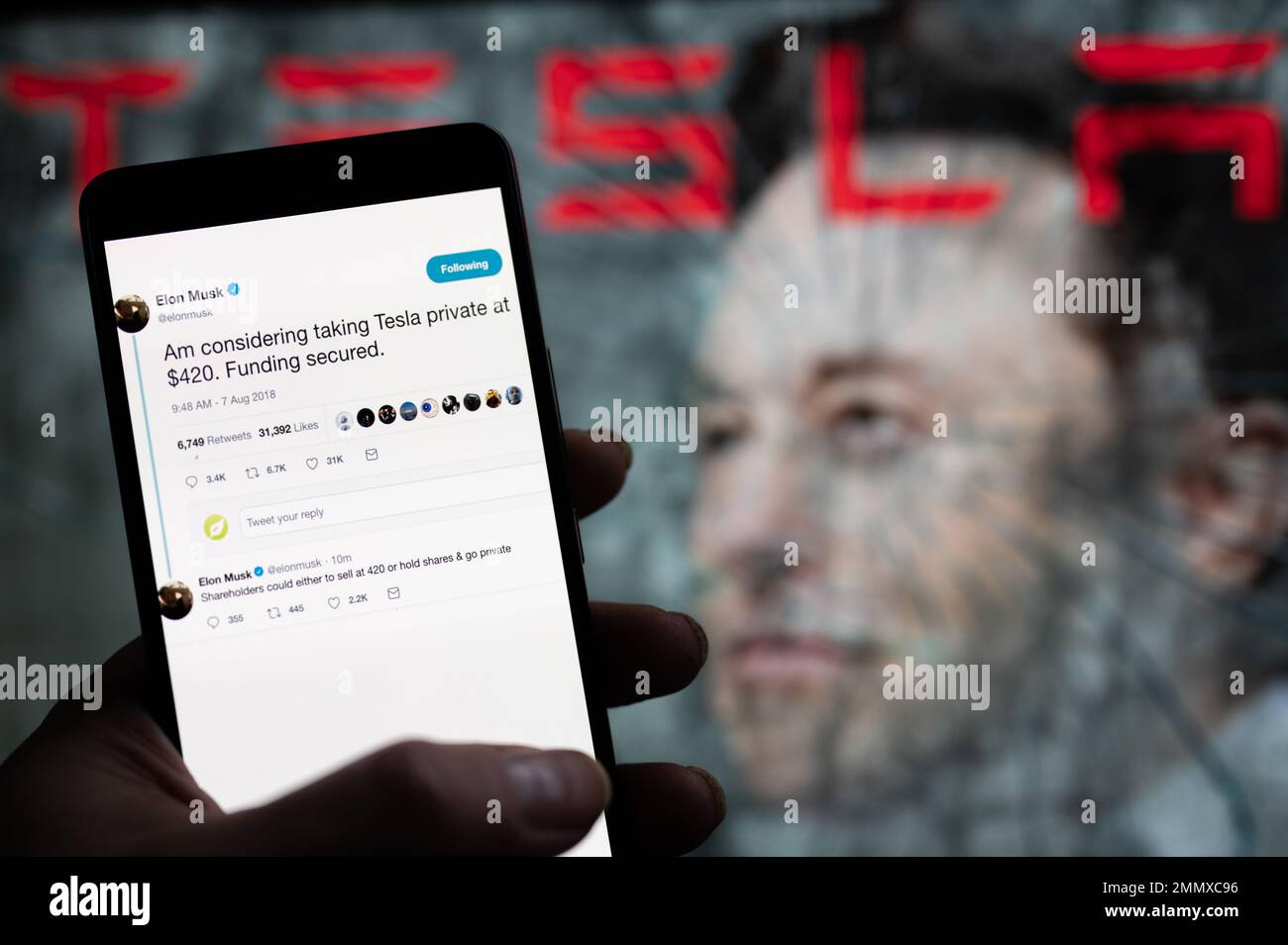 Elon Musk Tesla tweet displayed on mobile with in the background Elon ... Elon Musk Tesla tweet displayed on mobile with in the background Elon ...