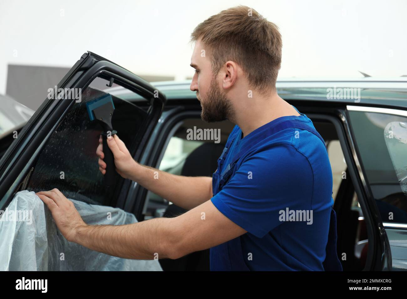 Worker washing tinted car window in workshop Stock Photo - Alamy