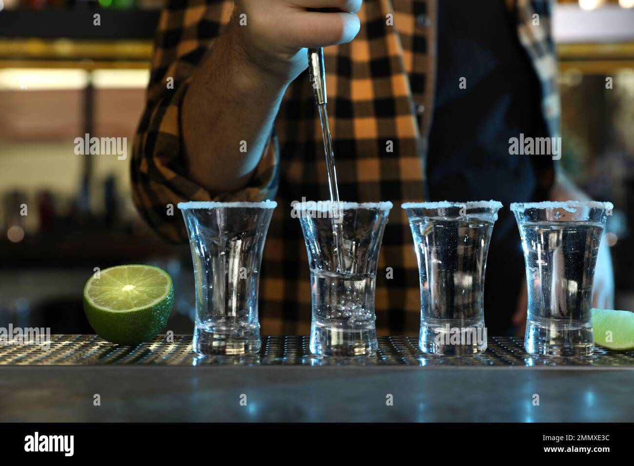 Bartender pouring Mexican Tequila into shot glasses at bar counter ...