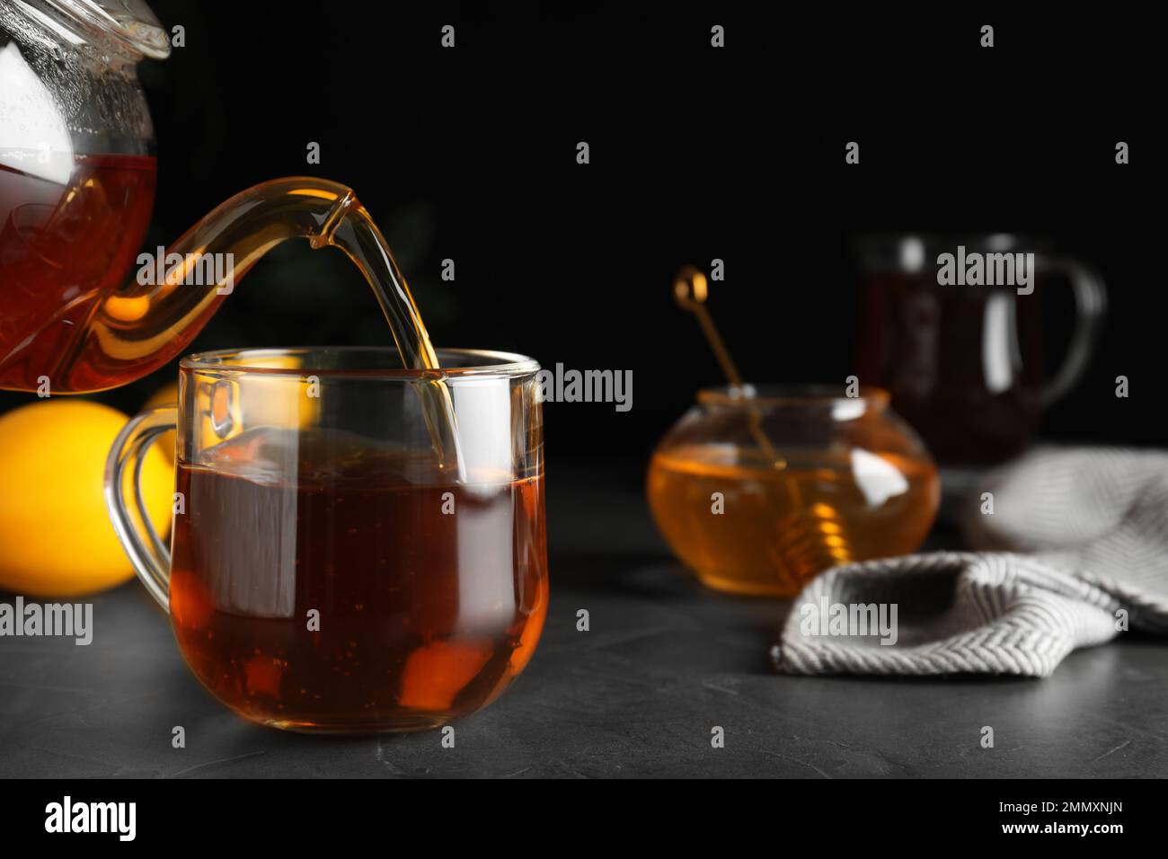 Delicious tea pouring into cup and honey on grey table Stock Photo - Alamy