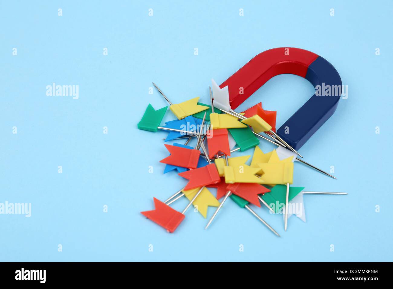 Magnet attracting colorful pins on light blue background Stock Photo ...