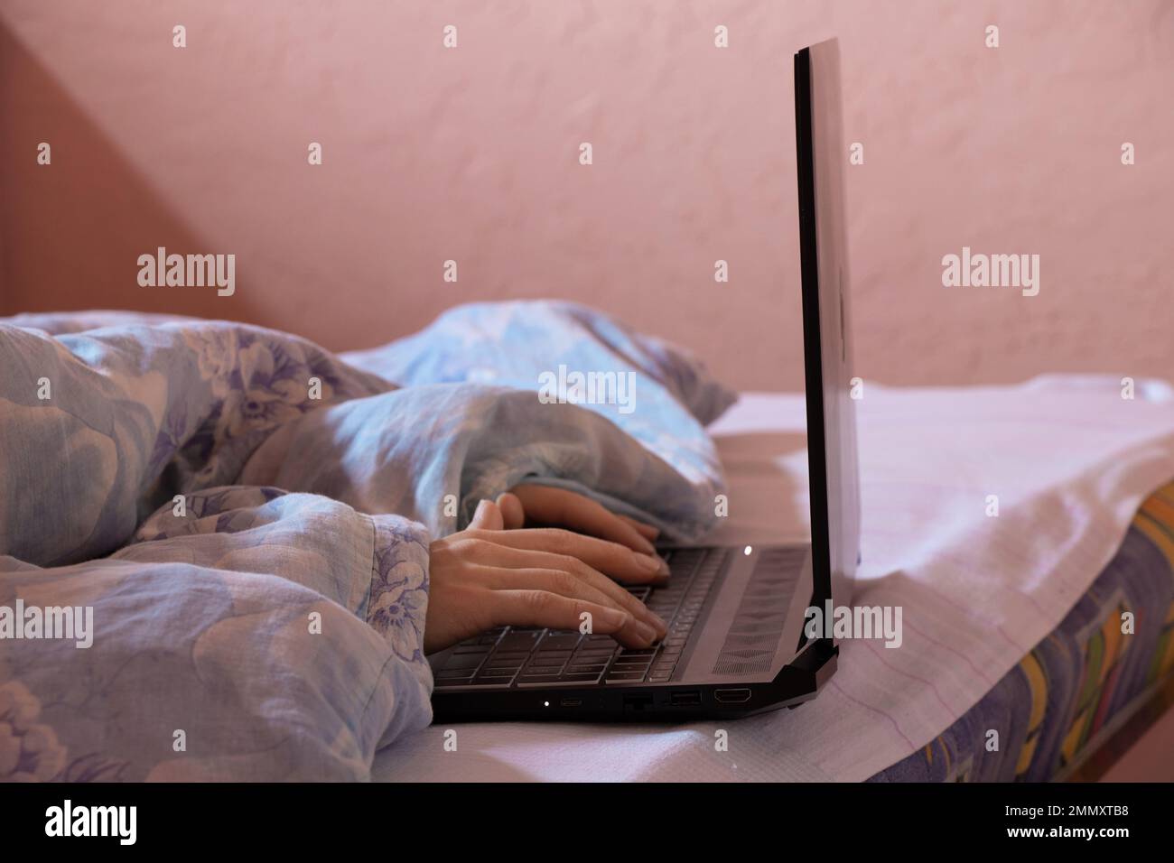 female hands on the laptop keyboard on the bed in a blanket, working at ...