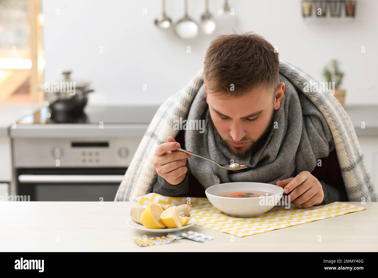 Sick young man eating tasty soup to cure flu at table in kitchen Stock ...
