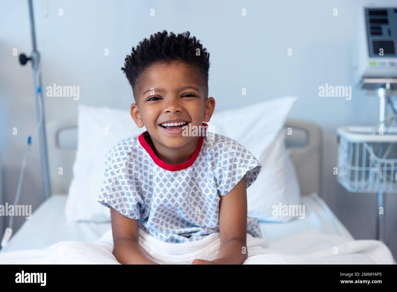 Happy african american boy patient sitting up in hospital bed, smiling ...