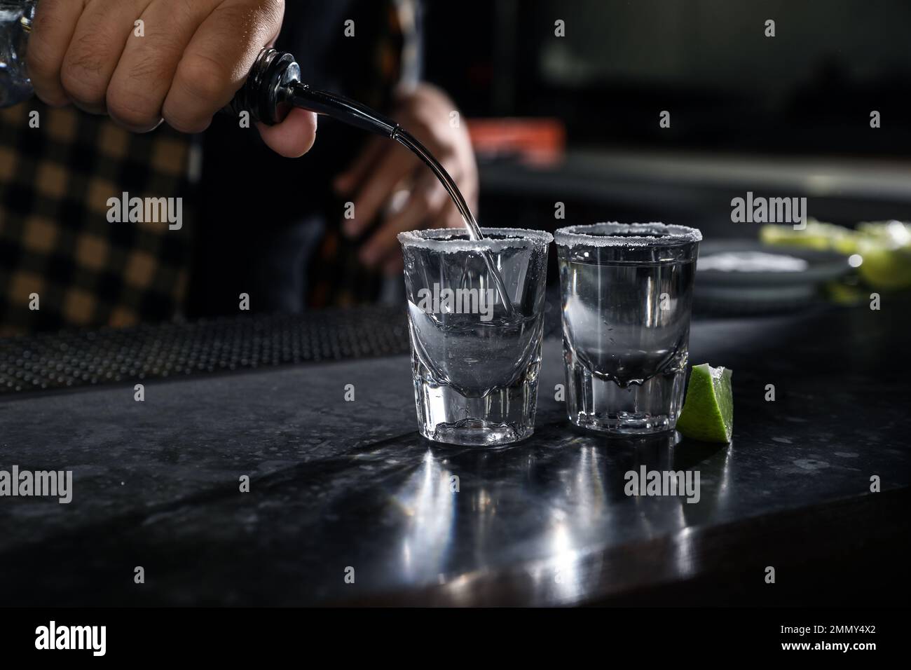 Bartender pouring Mexican Tequila into shot glasses at bar counter ...