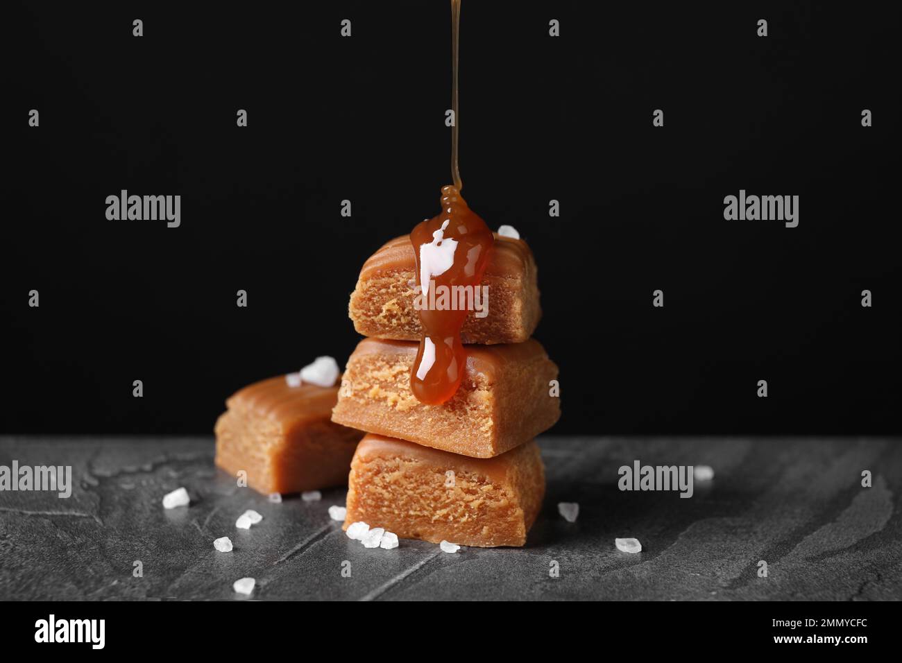 Pouring delicious salted caramel on candies against black background ...