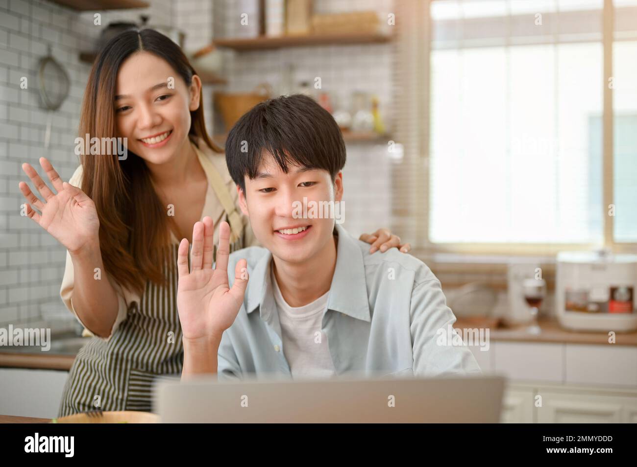 Happy and smiling young Asian couple waving hands, saying hi to their ...