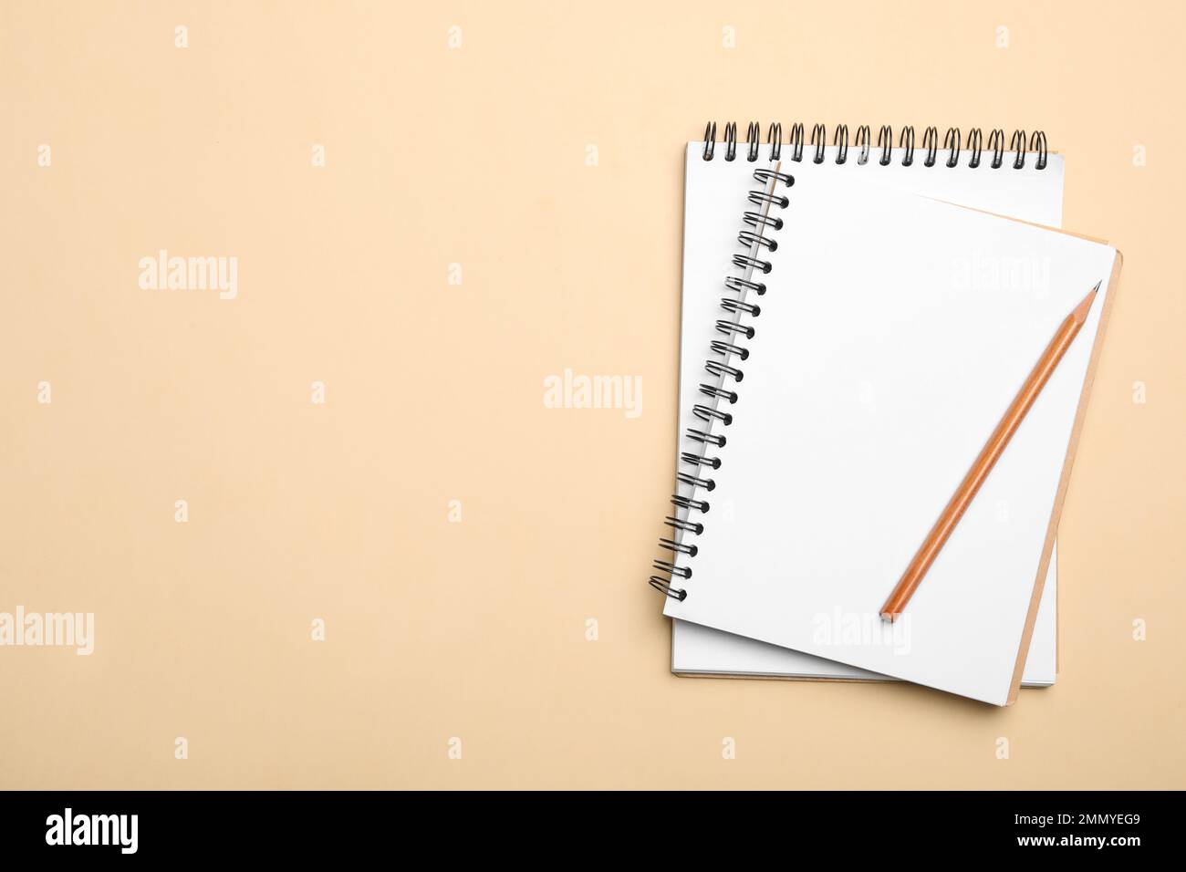 Open notebooks and pencil on beige background, top view. Space for text ...