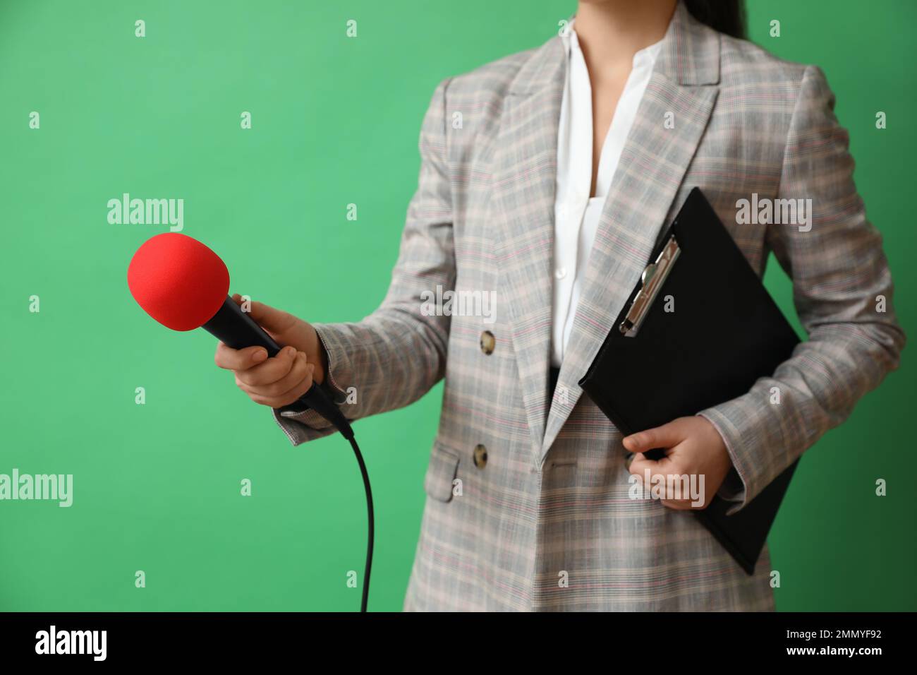Journalist with microphone and clipboard on green background, closeup ...