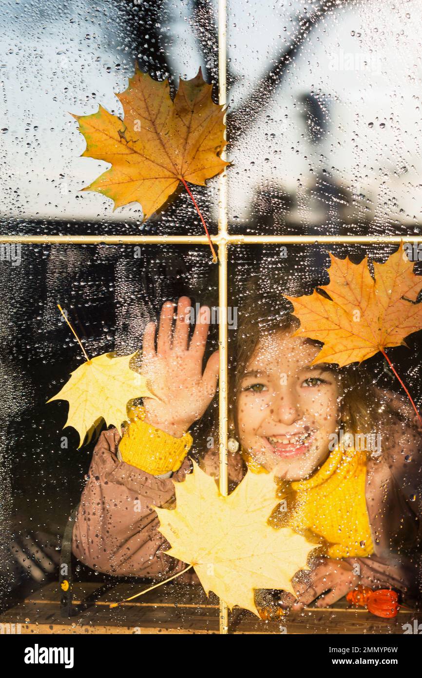 Child looks out of the window of the house outside, autumn weather, wet ...