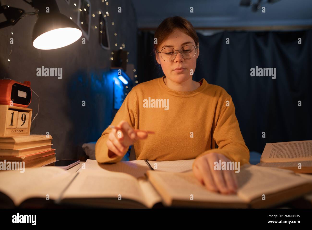 Focused student surrounded by books studying in dormitory at night ...