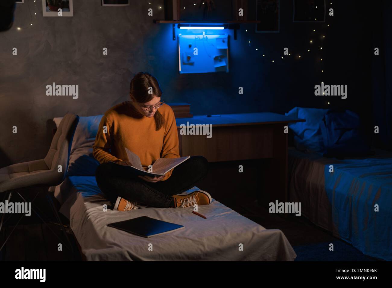 Female university student with long hair sitting on bed doing homework ...