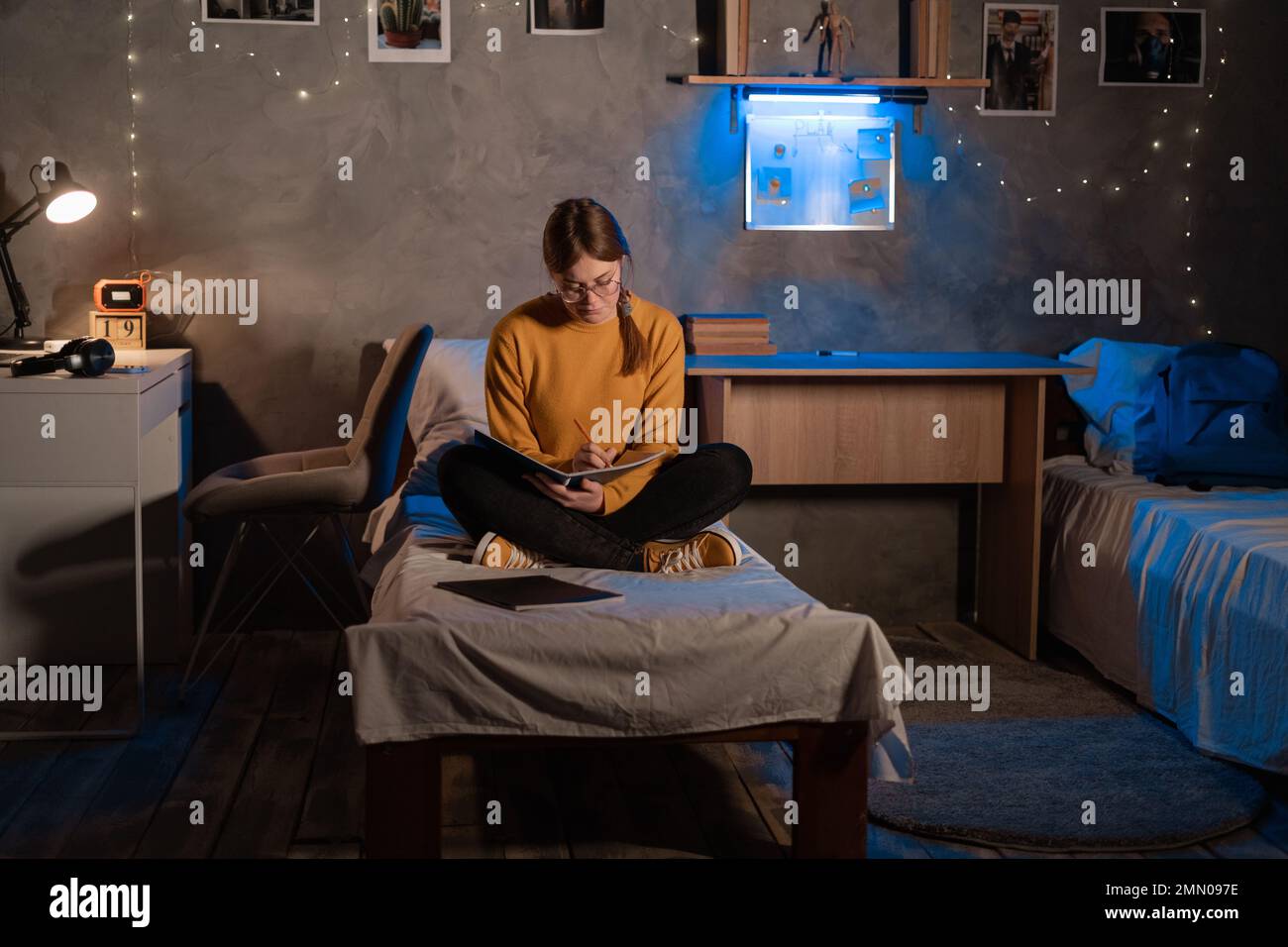 Female college student sitting on bed doing homework using copybooks ...
